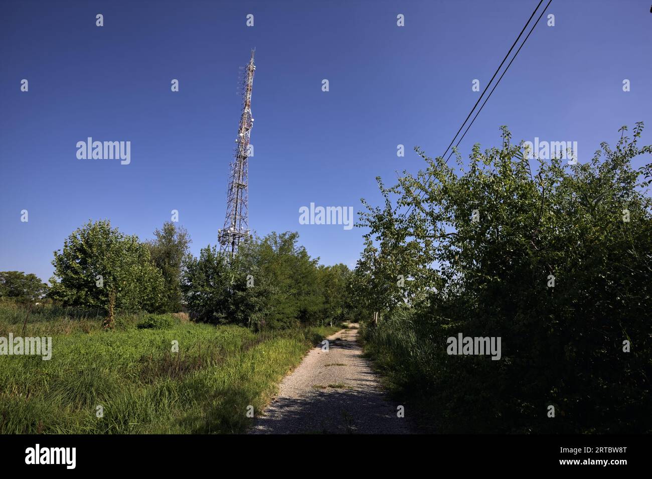 Narrow country road next to trees with an antenna in the background in ...