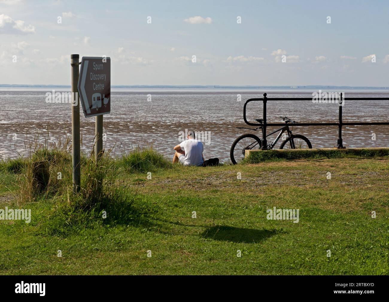 Young man sitting, looking out across the Humber estuary, at Kilnsea ...