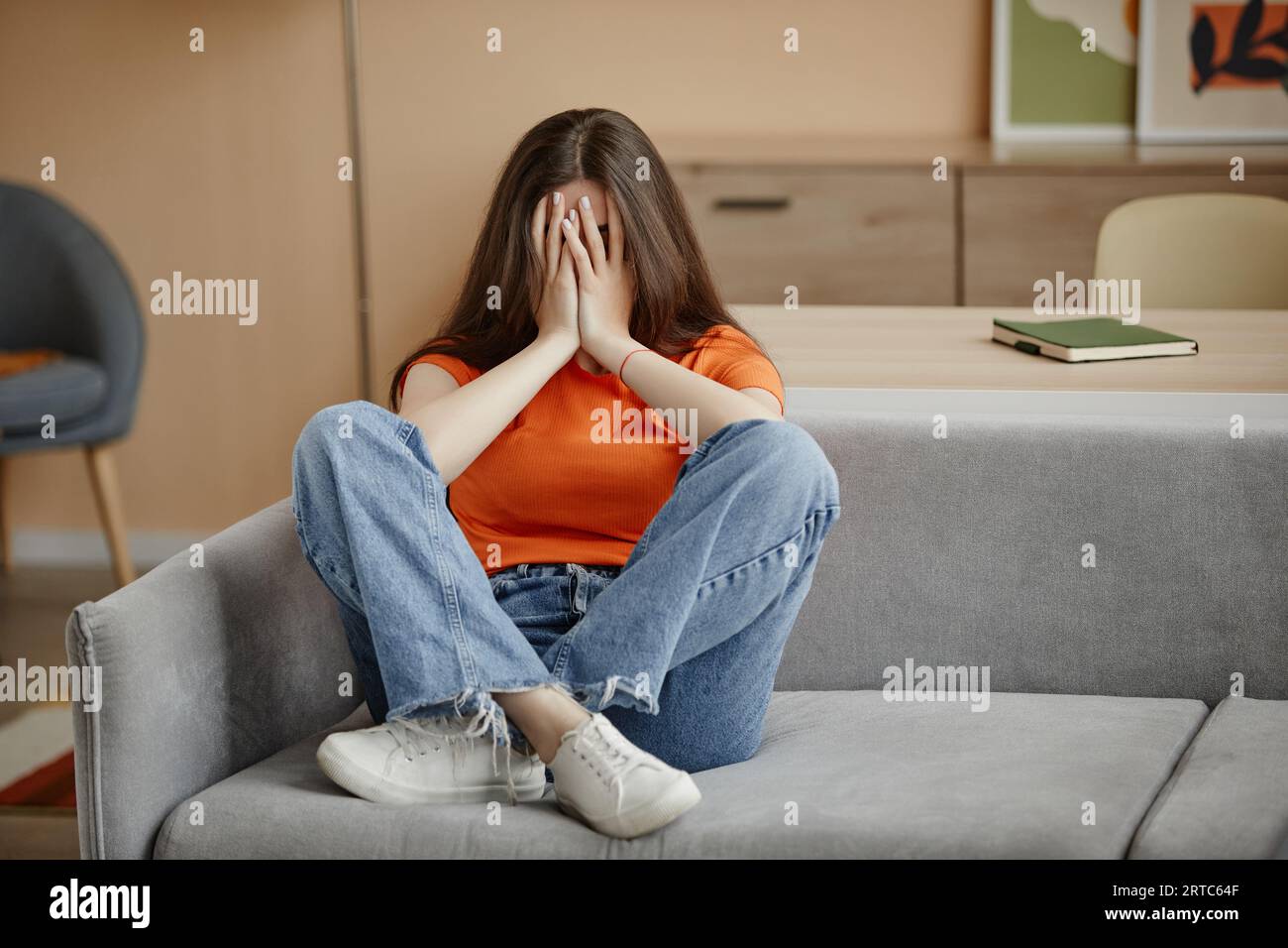 Full length portrait of crying young woman sitting on couch alone at ...