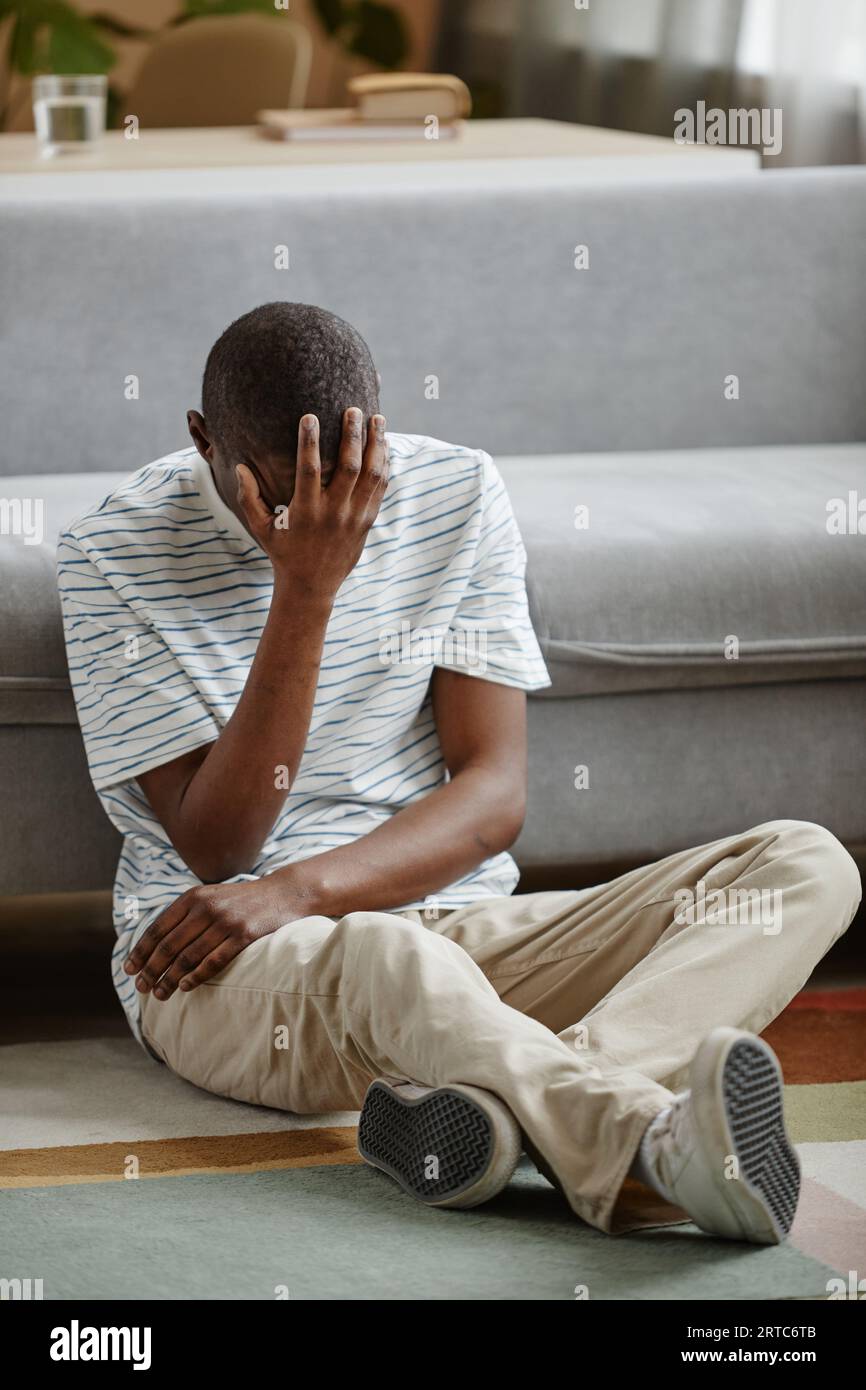 Vertical portrait of Black man crying on floor at home suffering from ...