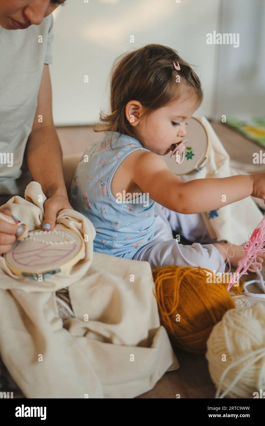 Mother sitting near her daughter on the floor, teaching child crafting ...