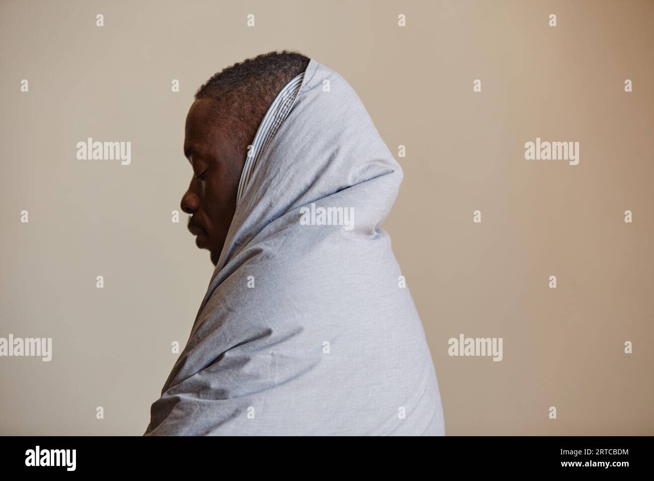 Minimal side view portrait of depressed Black man wrapped in blanket ...