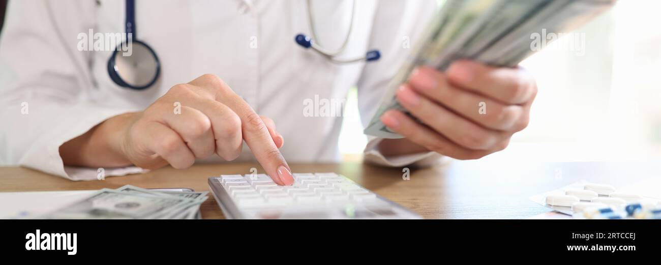 Doctor counting money while sitting at medical clinic desk with ...