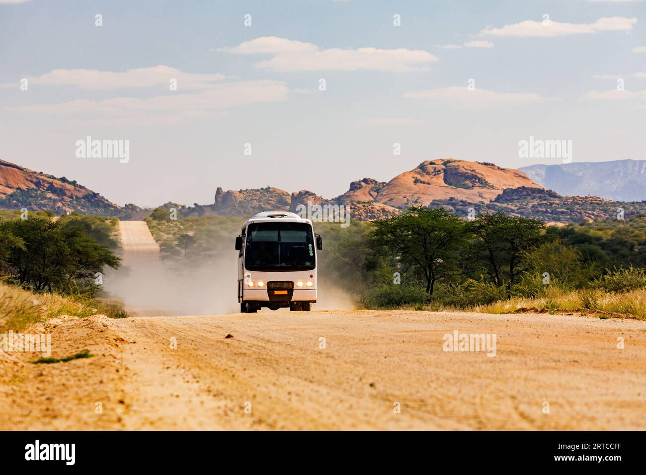 A modern bus for tourists drives on a dusty gravel road through the ...