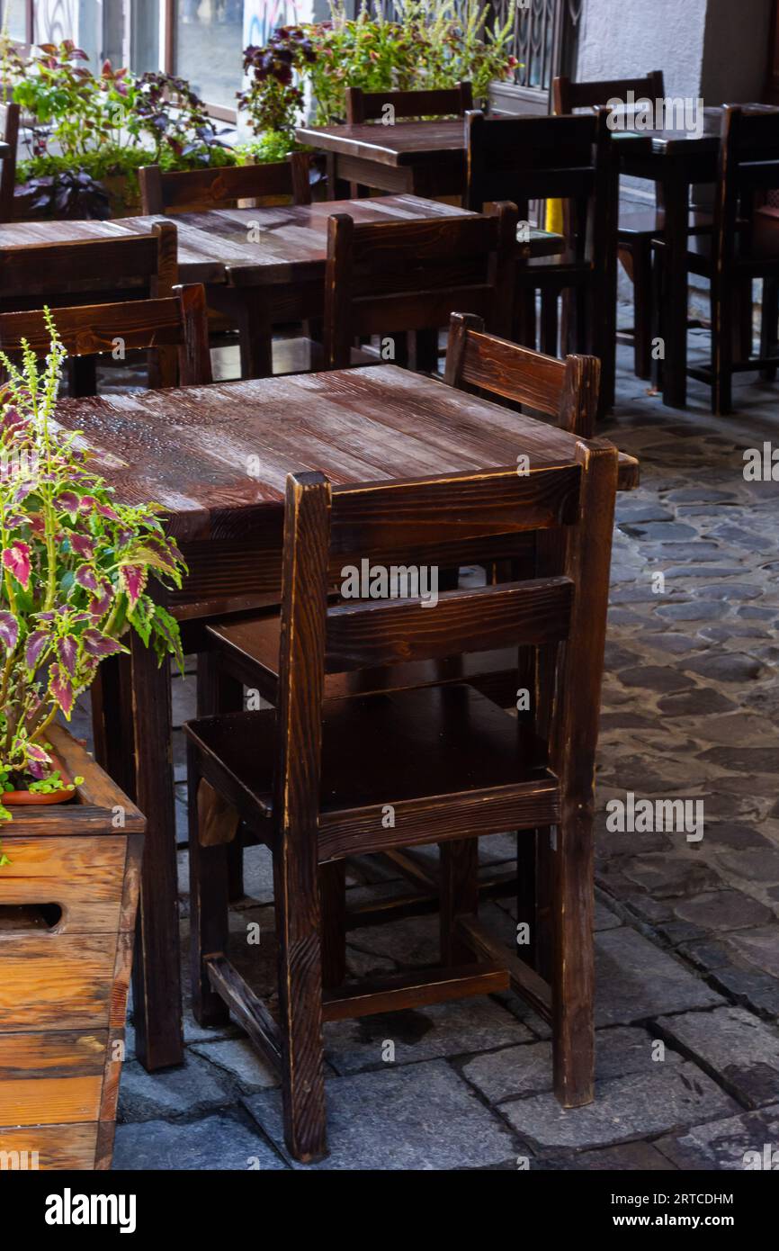 Empty wet wooden table and chairs on terrace of outdoor cafeteria ...