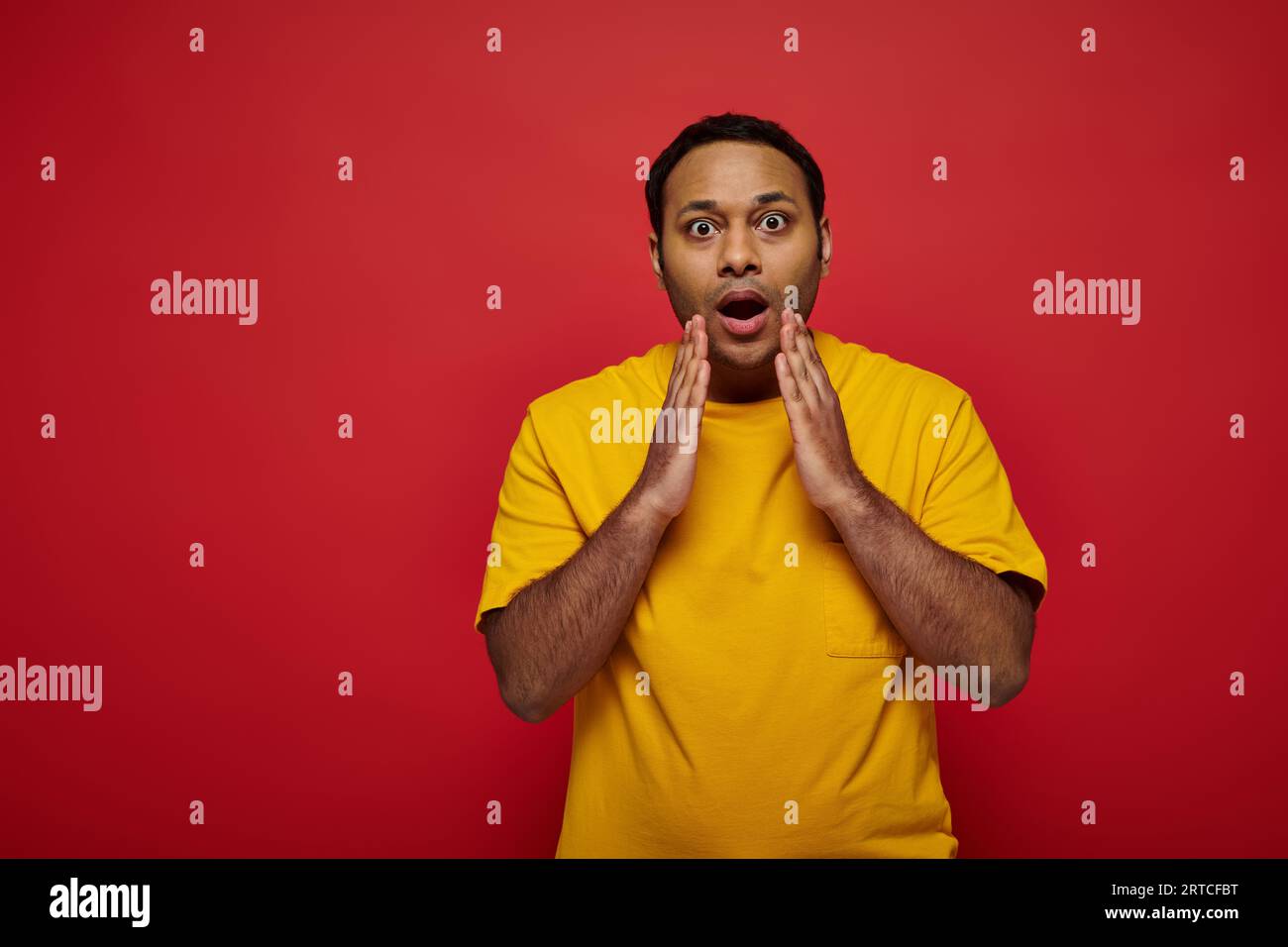 shocked indian man in bright casual clothes looking at camera on red ...