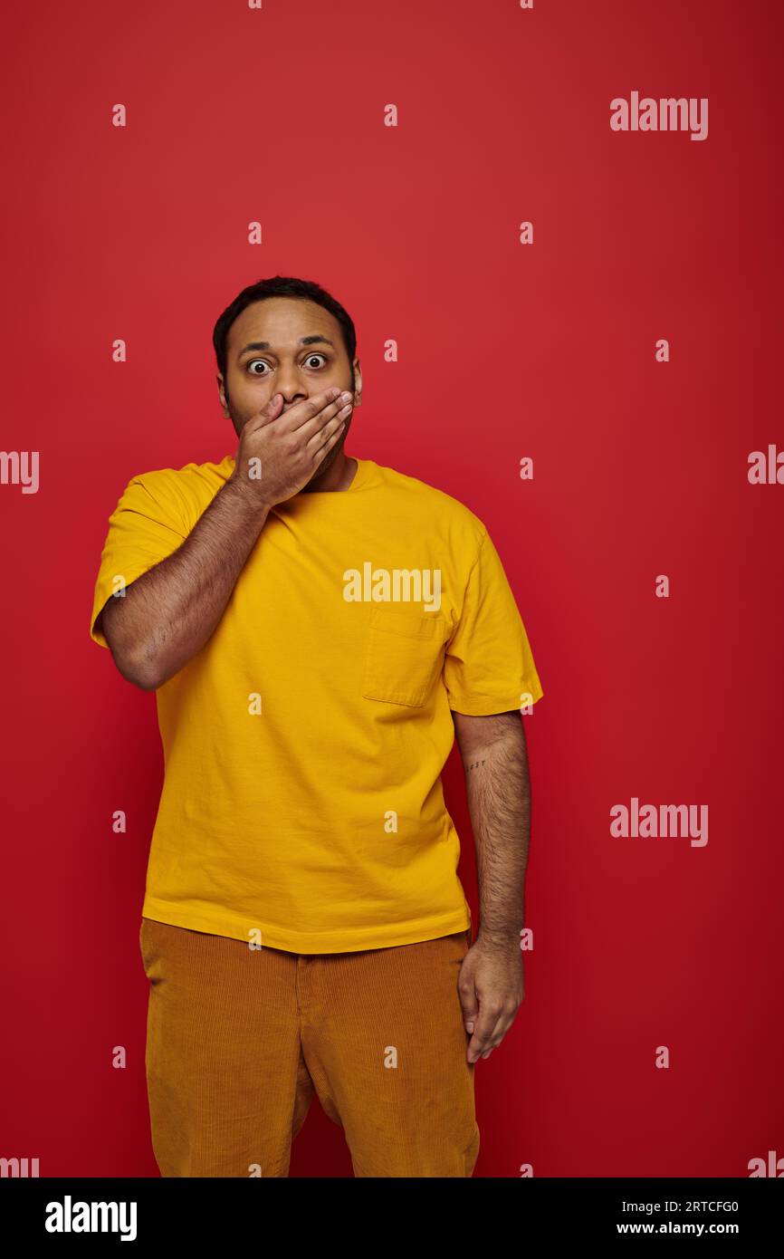 shocked indian man in bright clothes covering mouth and looking at ...
