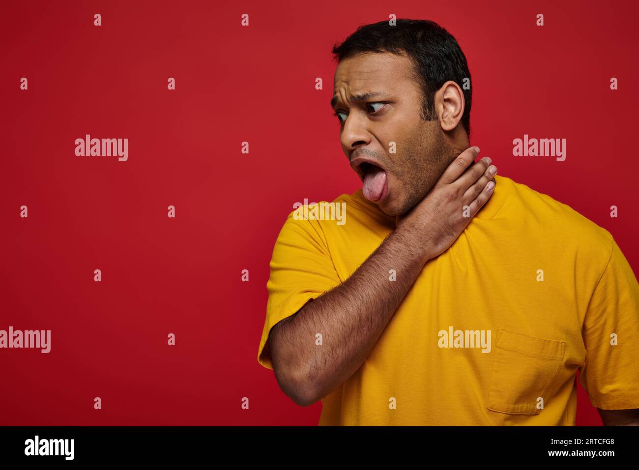 indian man in yellow clothes sticking out tongue while choking on red ...