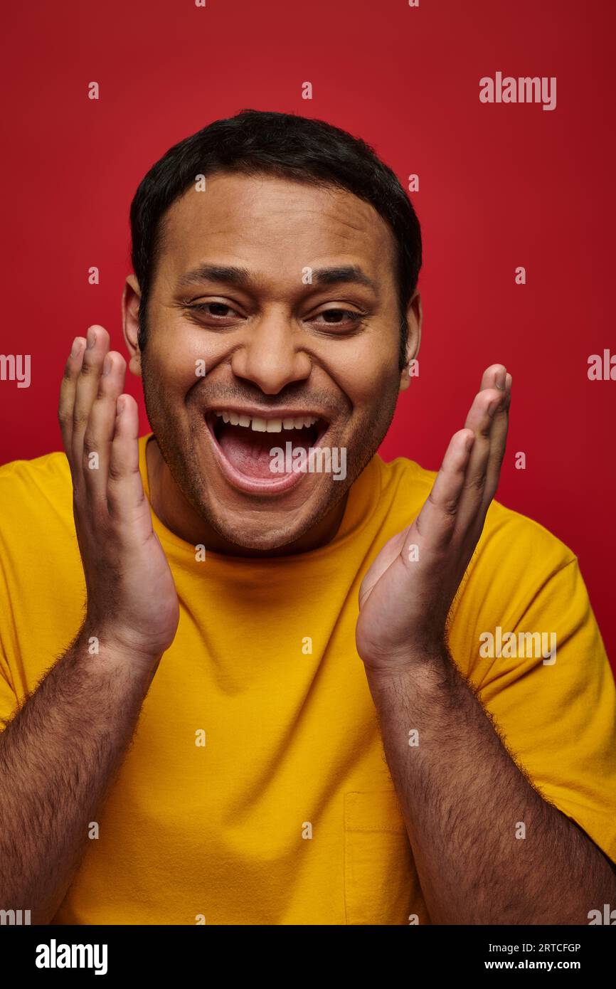 face expression, excited indian man in yellow t-shirt gesturing on red ...