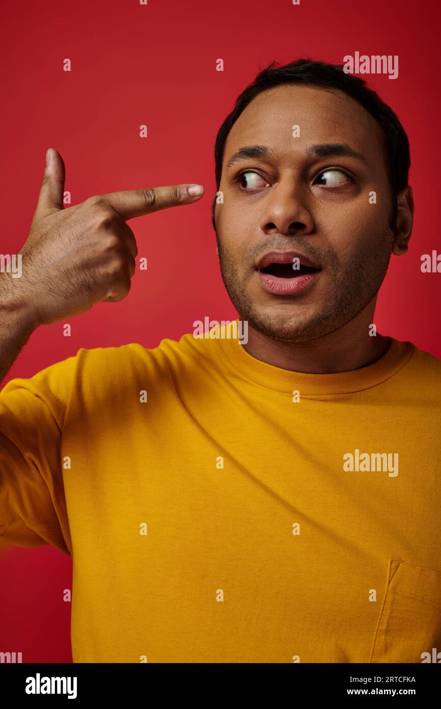 shocked indian man in yellow t-shirt pointing with finger at head on ...