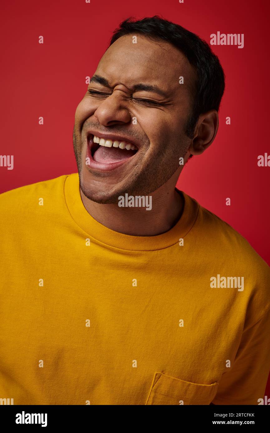 face expression, excited indian man in yellow t-shirt laughing on red ...