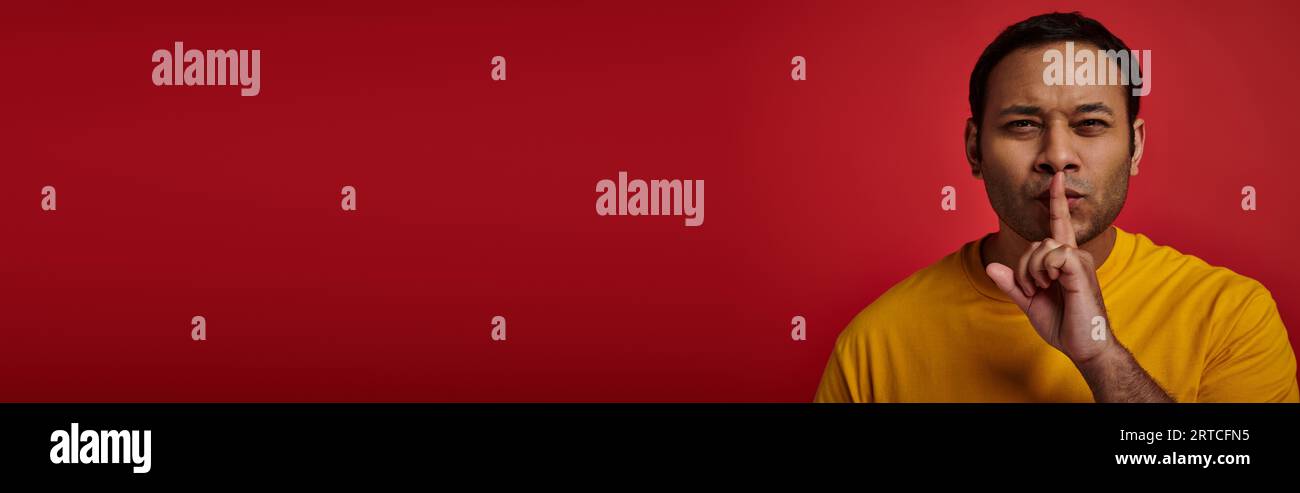 indian man in yellow t-shirt showing shh gesture on red backdrop ...