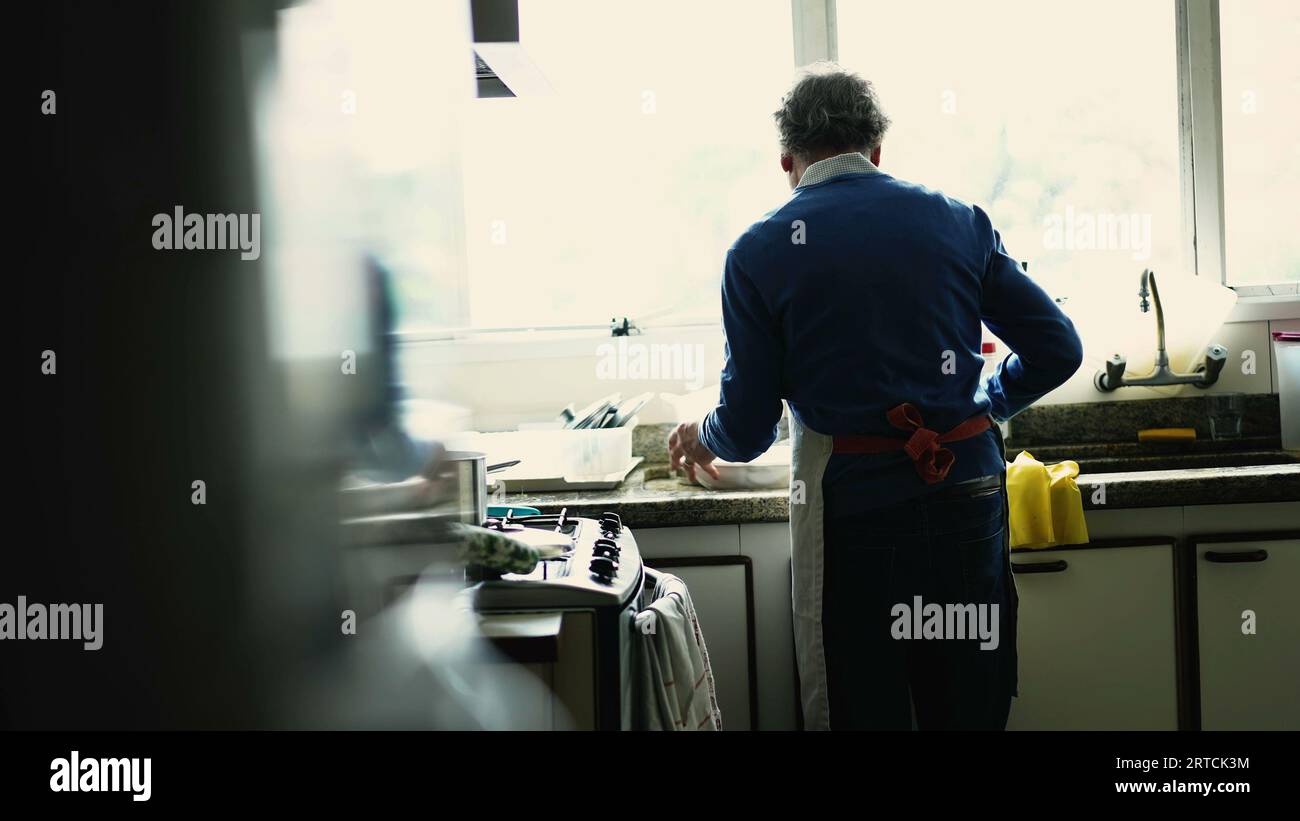 Back of senior man by kitchen sink preparing meal. Candid elderly cook ...