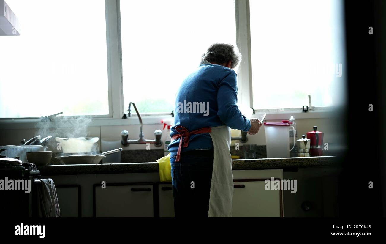 Back of senior chef standing by kitchen sink pouring food into plate ...