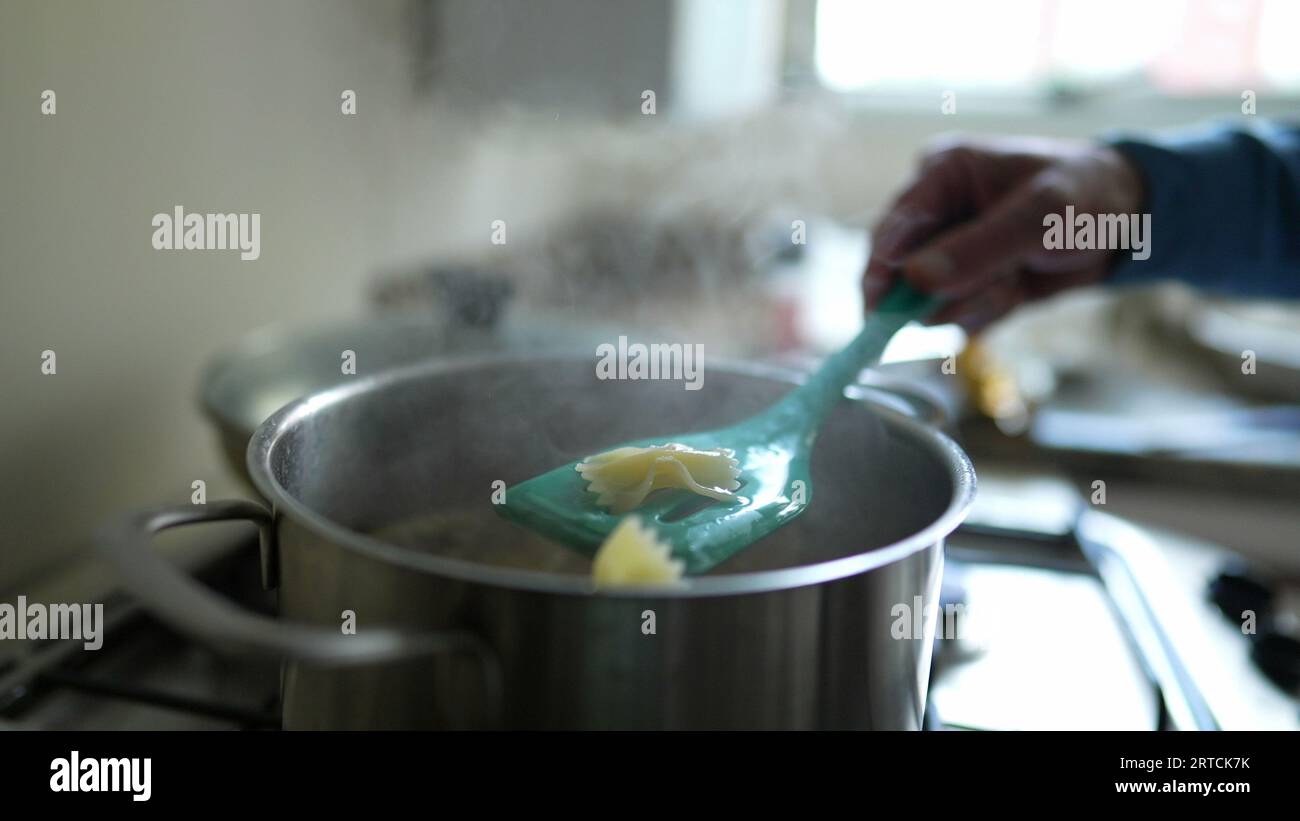 Close-up hand checking pasta inside metal pan to make sure it is al ...