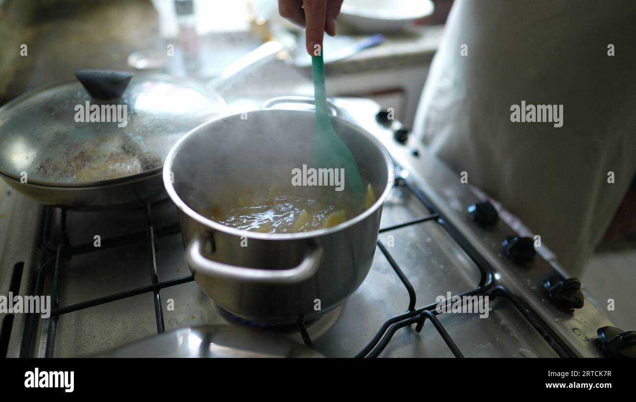 Close-up hand stirring food in boiling water inside metal pan at ...