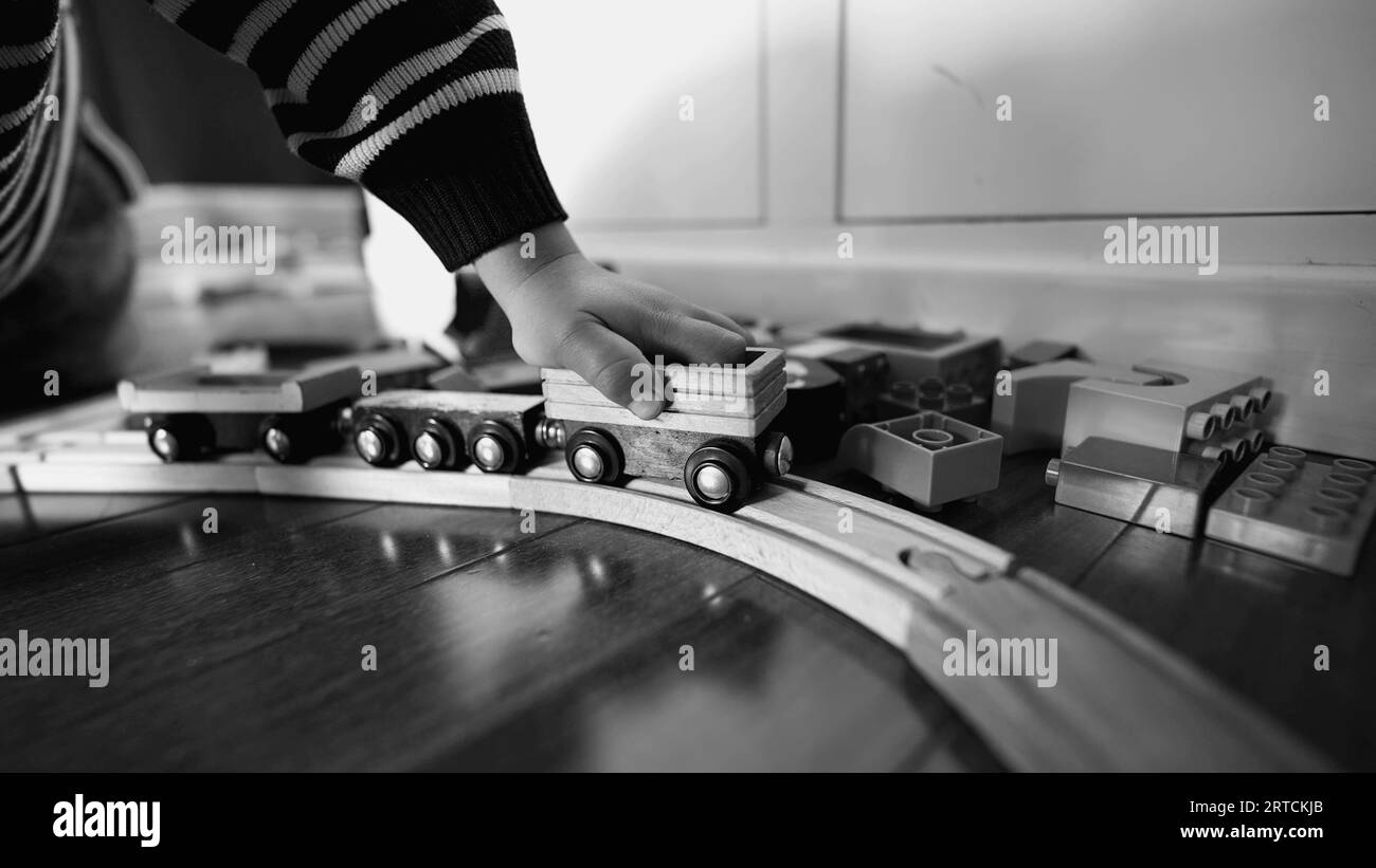 Child hand pushing vintage train wagon on wooden tracks in monochrome ...