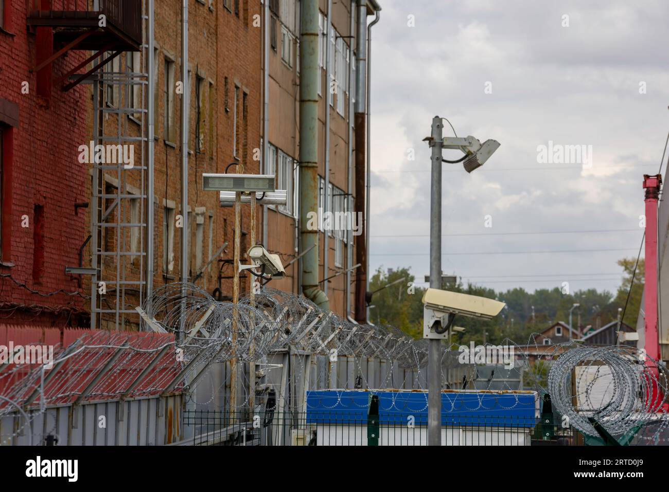 barb wire and surveillance cameras over fence in city near red brick ...