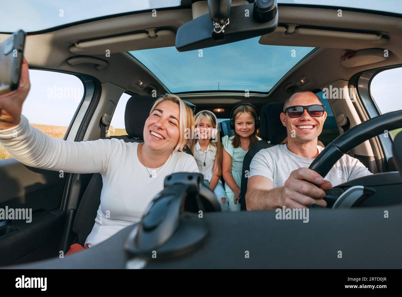 Happy young couple with two daughters inside car during auto trop. They are smiling, laughing ...