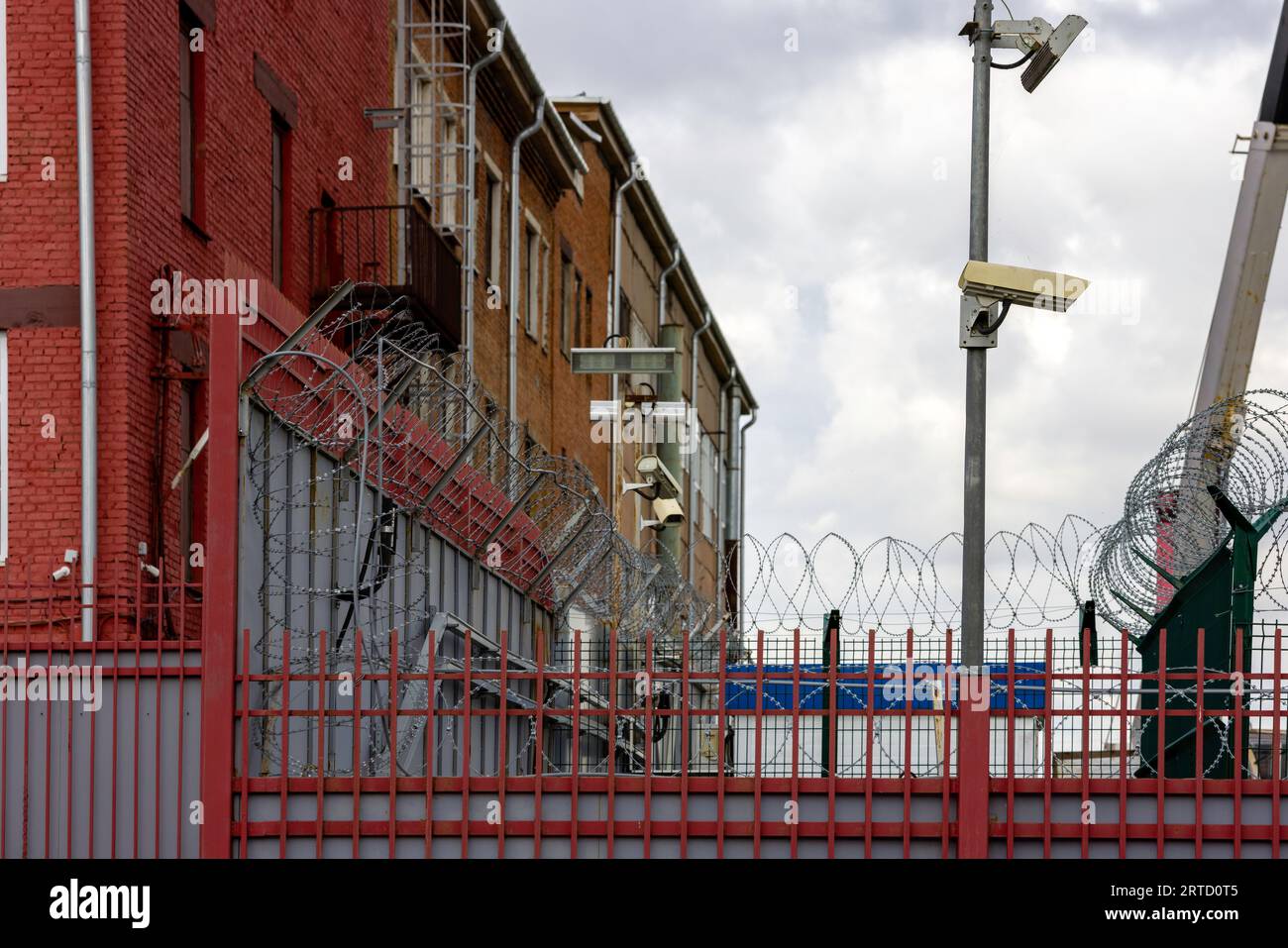 barb wire and surveillance cameras over fence in city near red brick ...