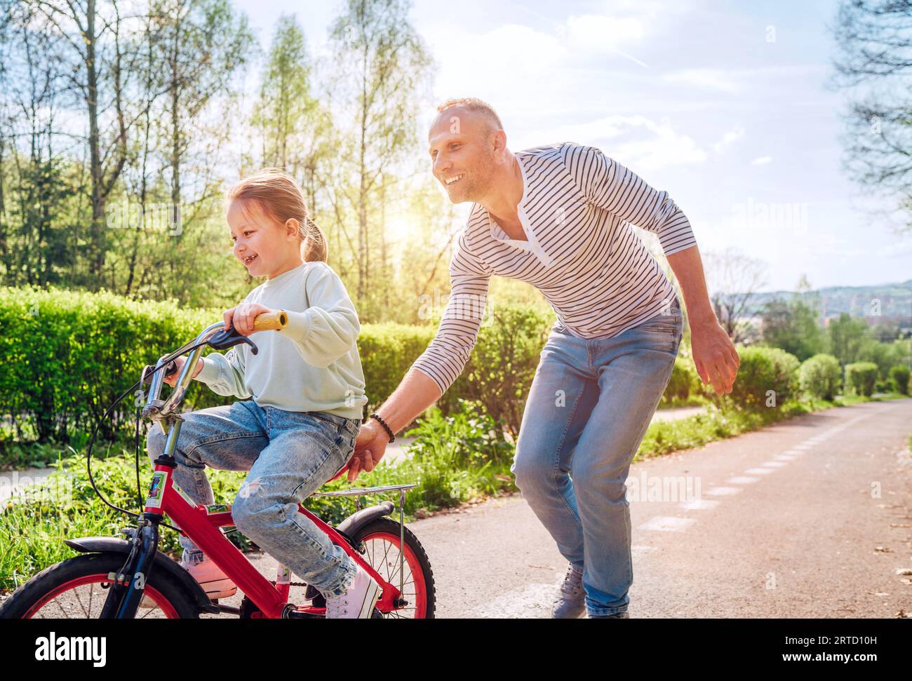 Smiling father teaching his daughter to ride a bicycle. They enjoy ...