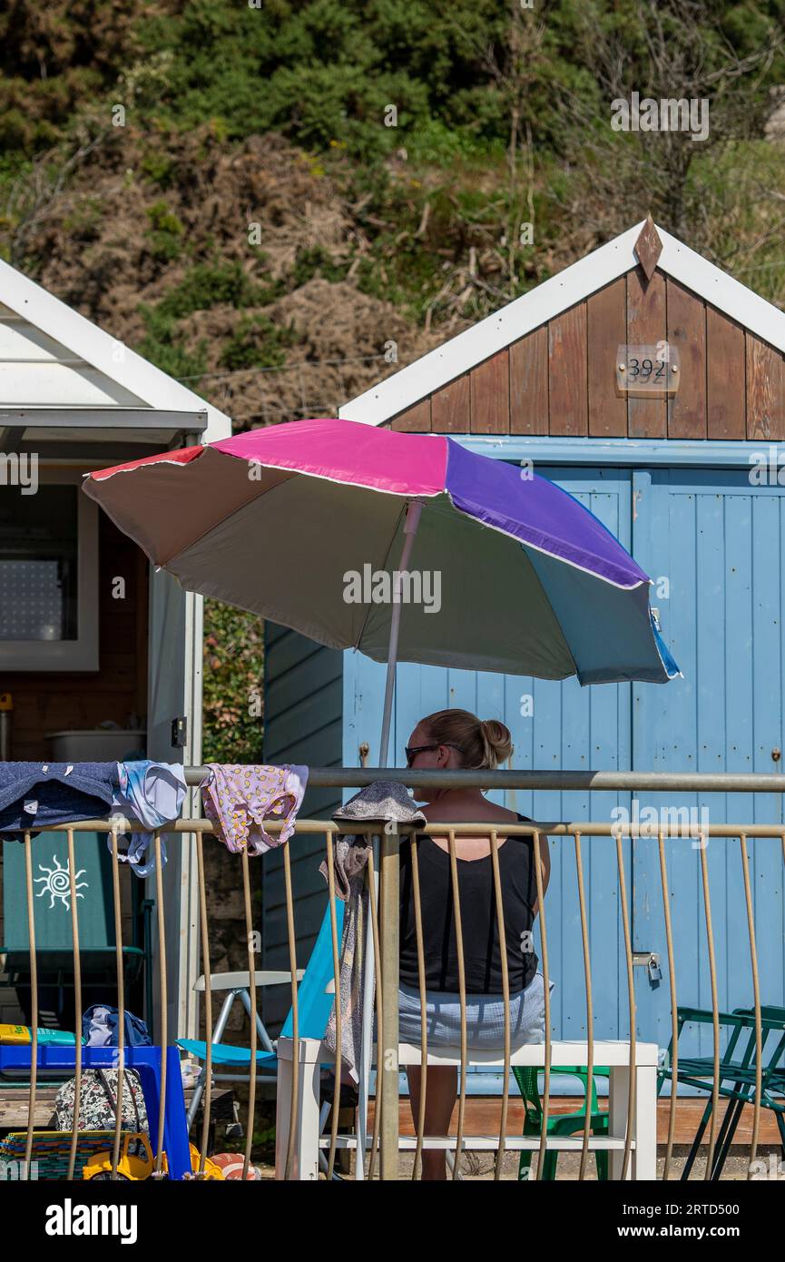 young woman sitting outside of a beach hut under a sunshade or parasol ...