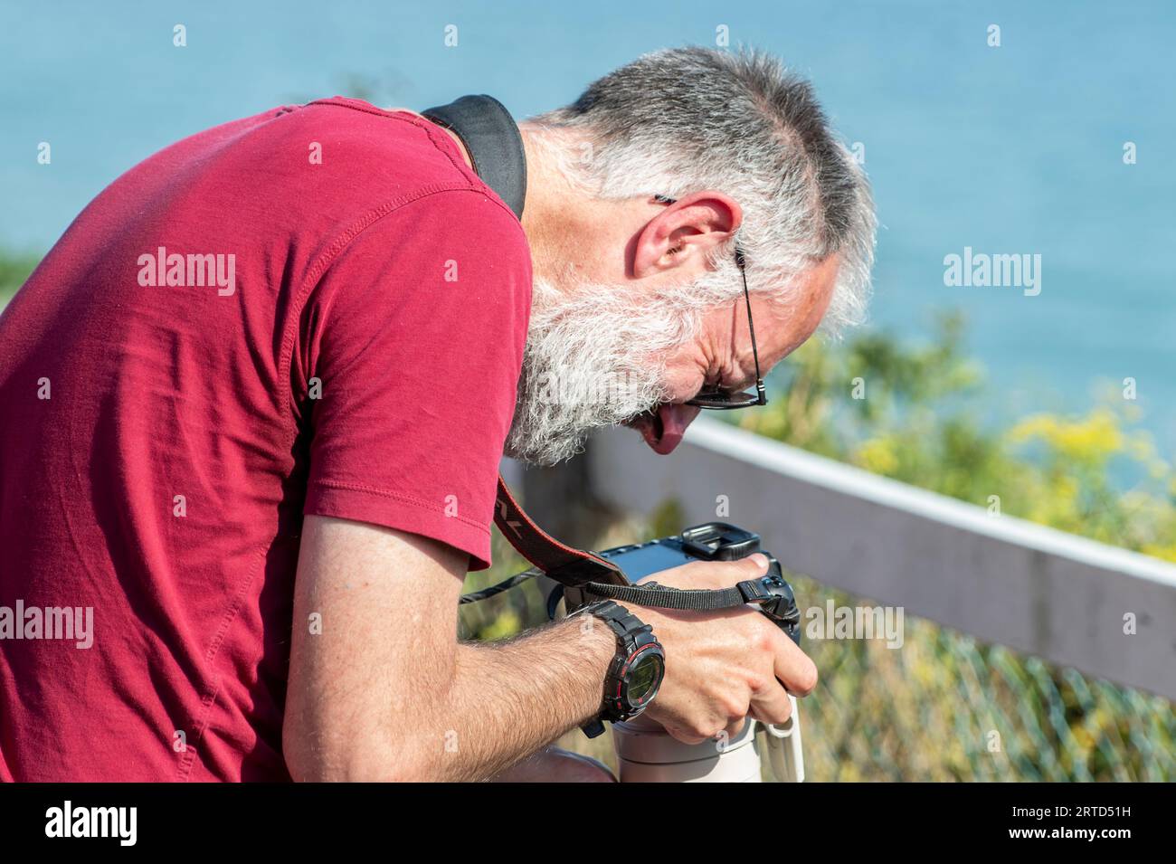 older man with grey hair looking at the back of a digital camera after ...