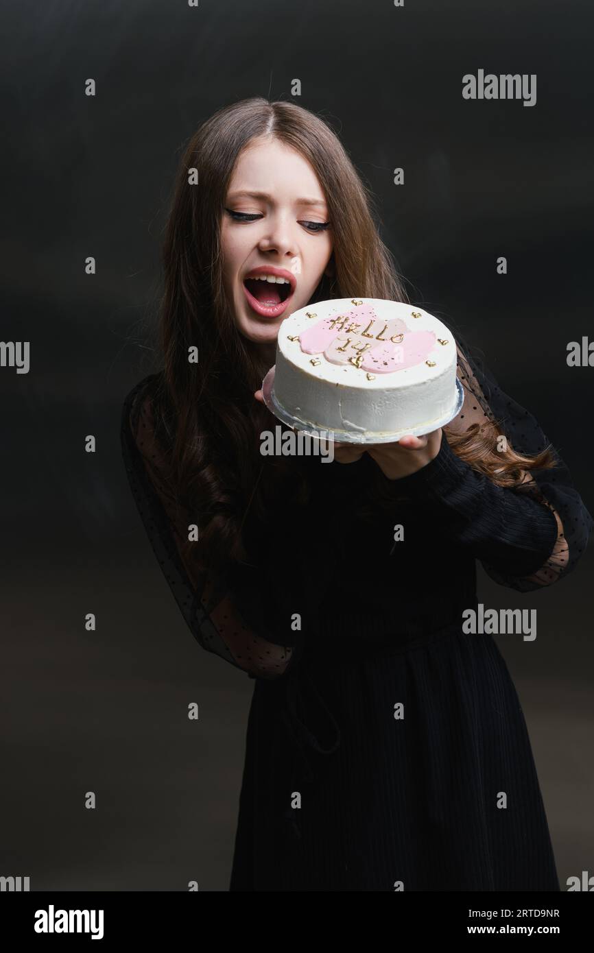 A teenage girl in a black dress holds a birthday cake with the ...