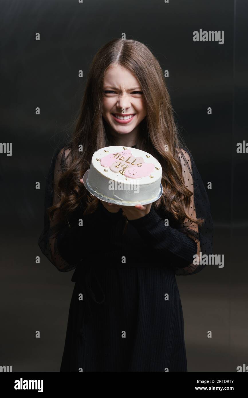 A teenage girl in a black dress holds a birthday cake with the ...