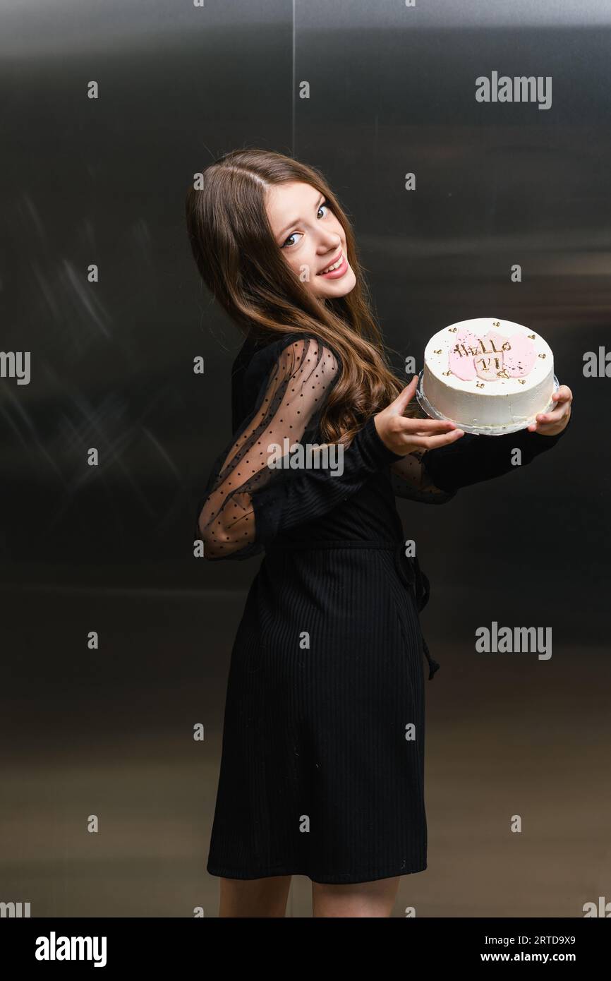 A teenage girl in a black dress holds a birthday cake with the ...