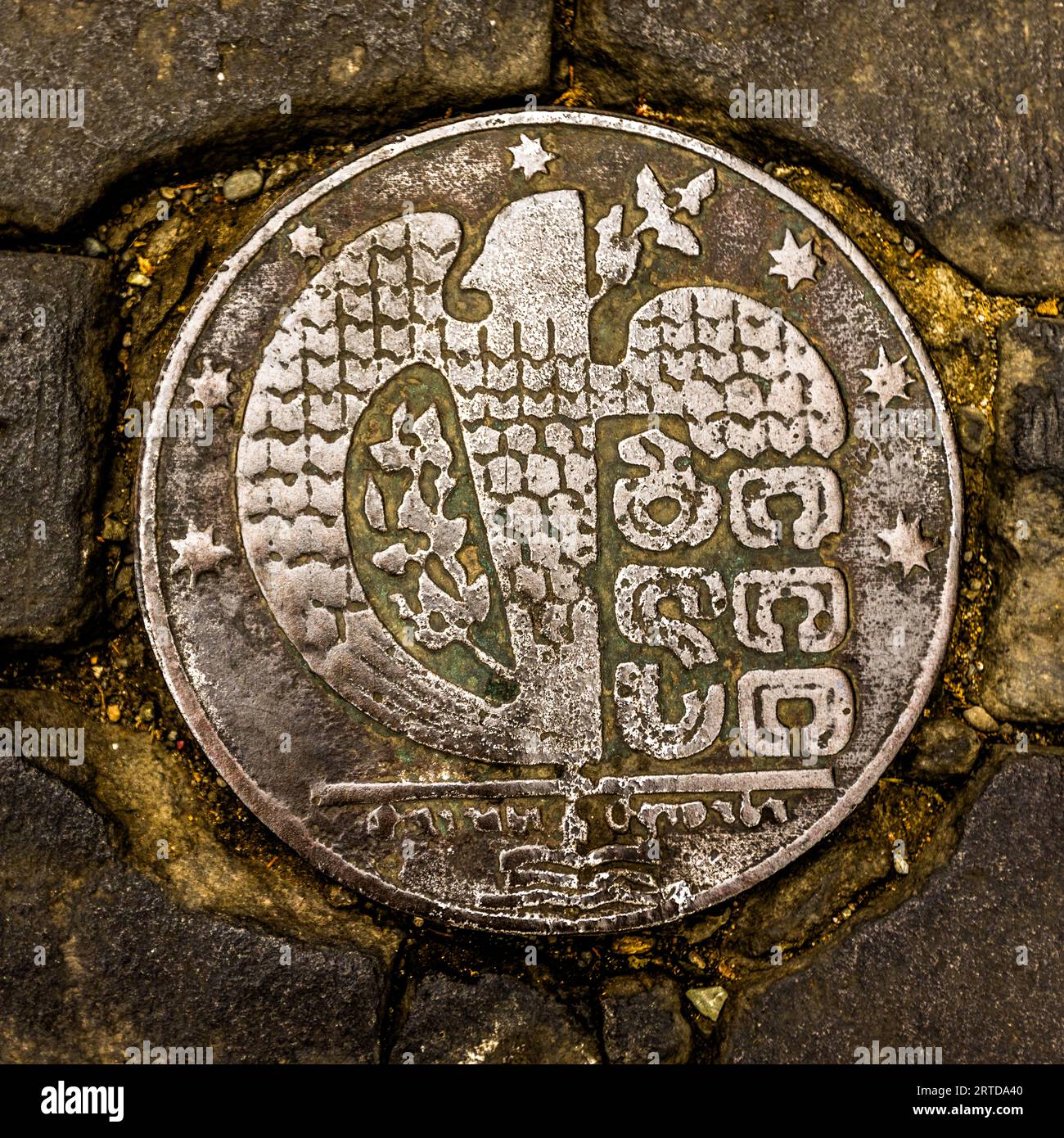 A round metal plaque is embedded in paving stones. It shows an eagle ...