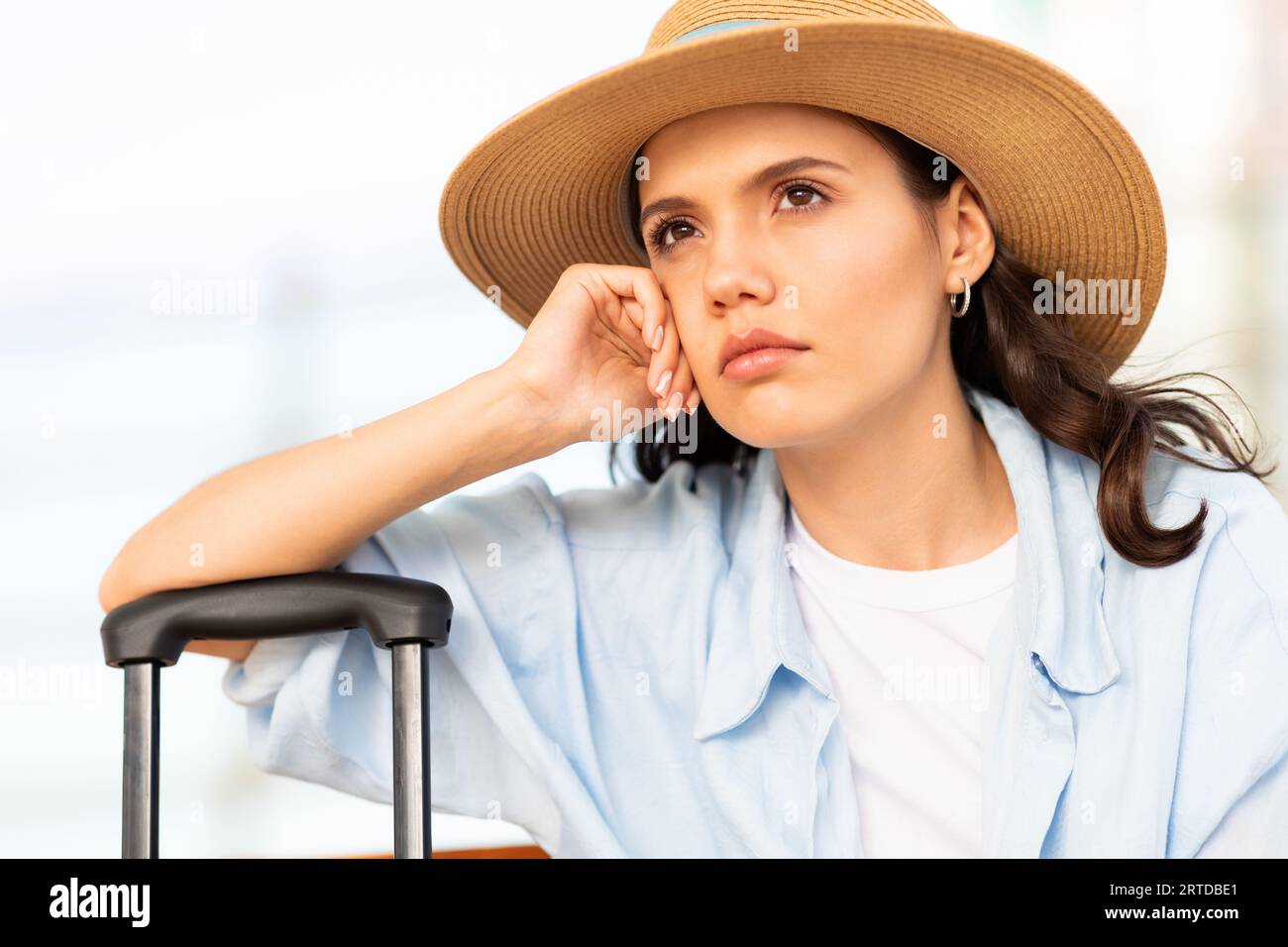 Unhappy sad young caucasian lady in hat with suitcase looks at empty ...