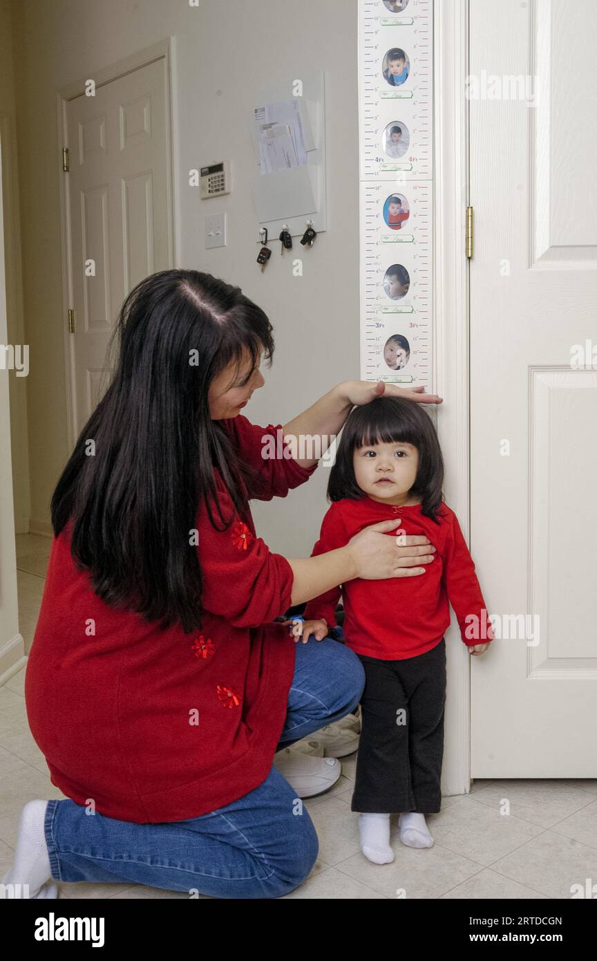 Asian mom measures their daughter on the family growth chart. Photo by ...