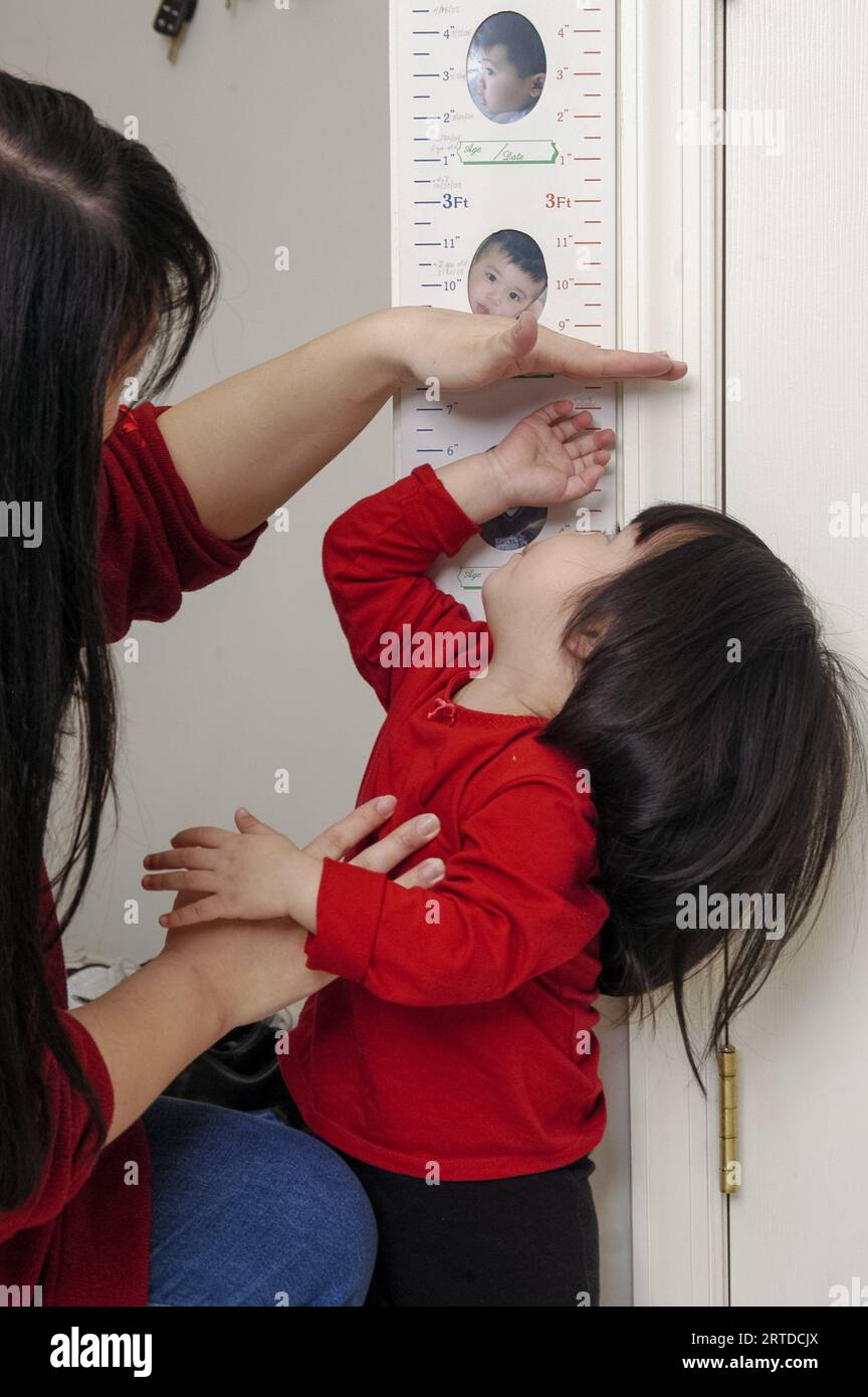 Asian mom measures their daughter on the family growth chart. Photo by ...