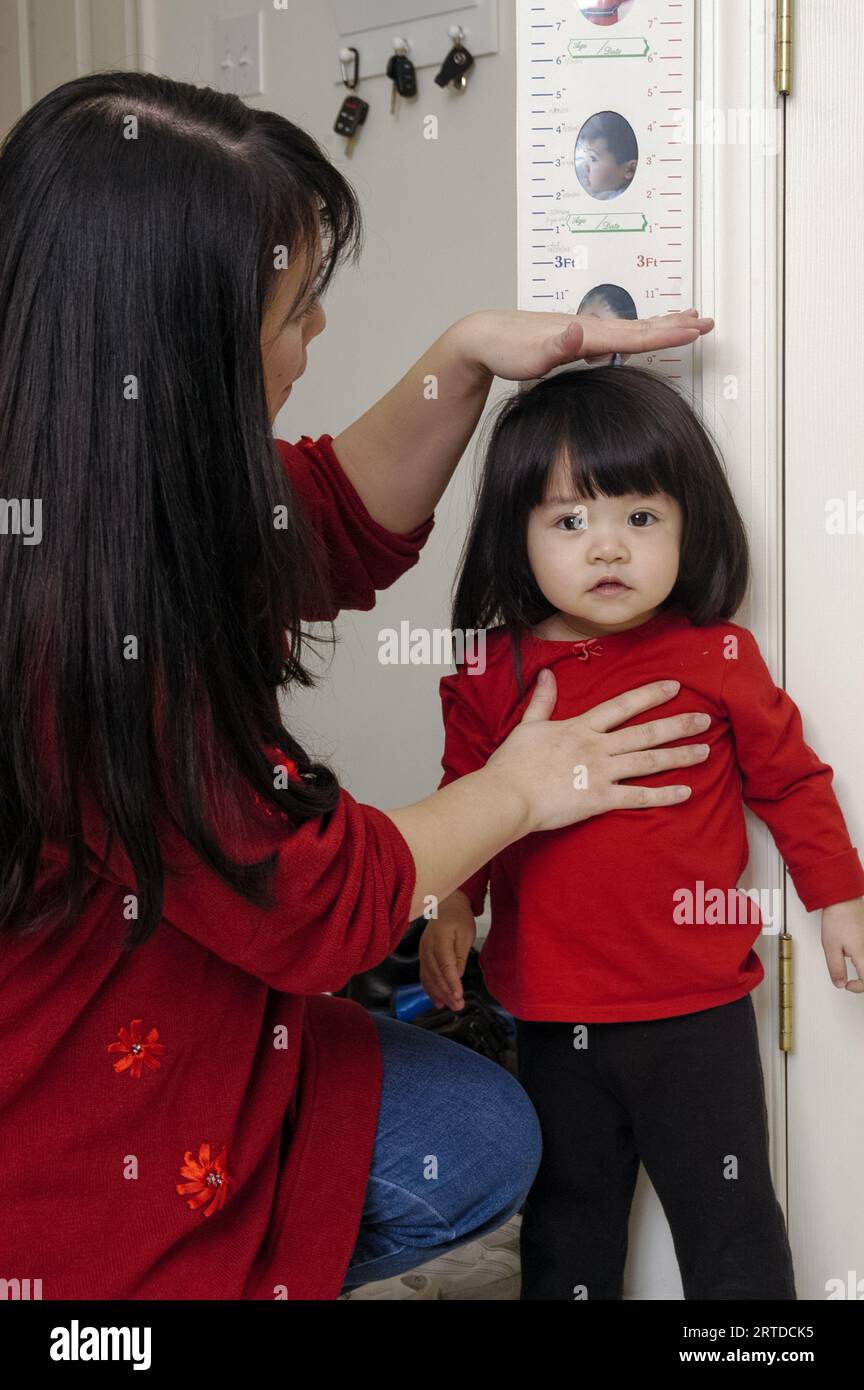 Asian mom measures their daughter on the family growth chart. Photo by ...