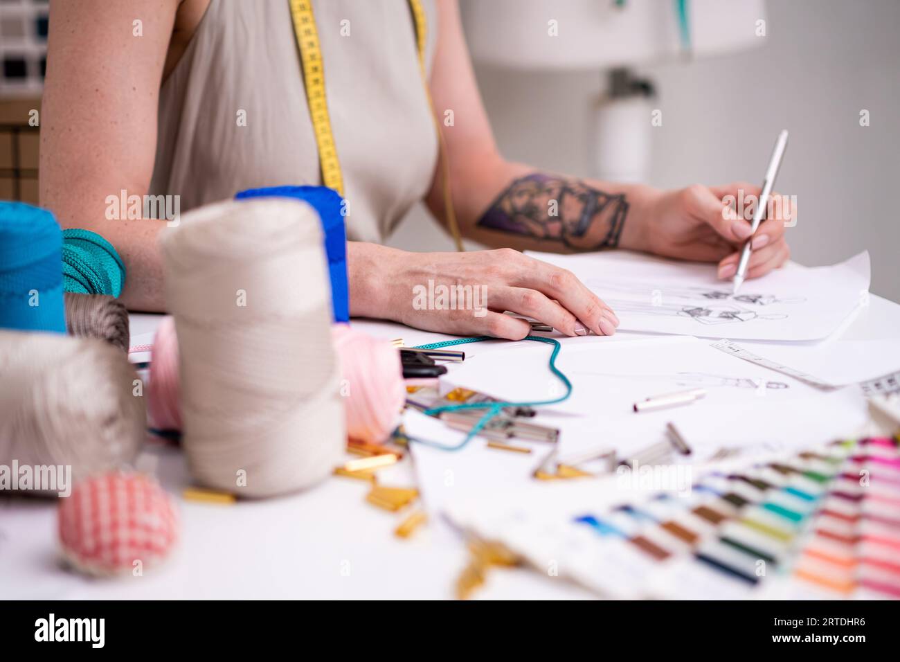 Tailor with tattoo draws dress sketch with pencil at desk in sewing ...