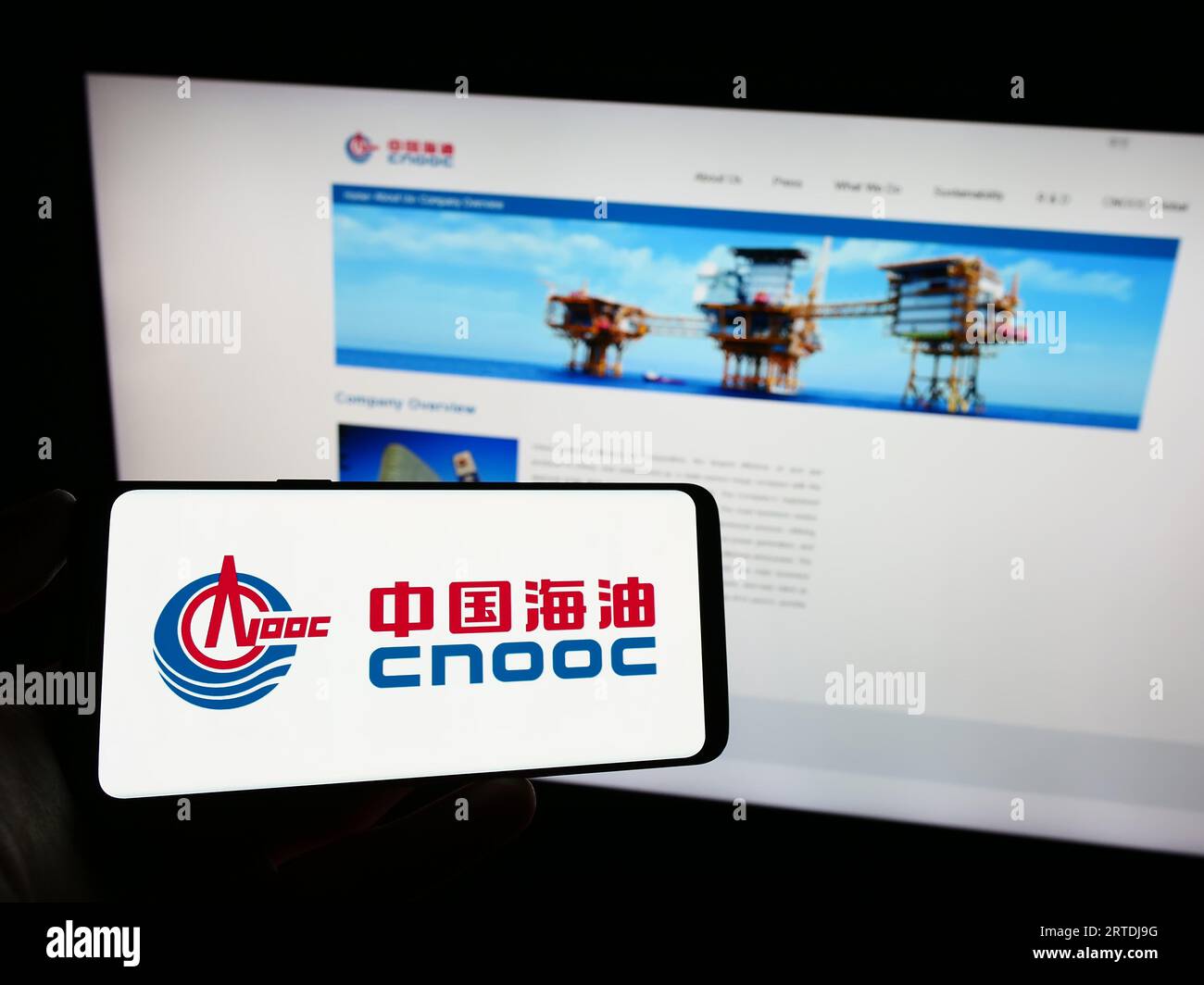 Person holding mobile phone with logo of China National Offshore Oil ...