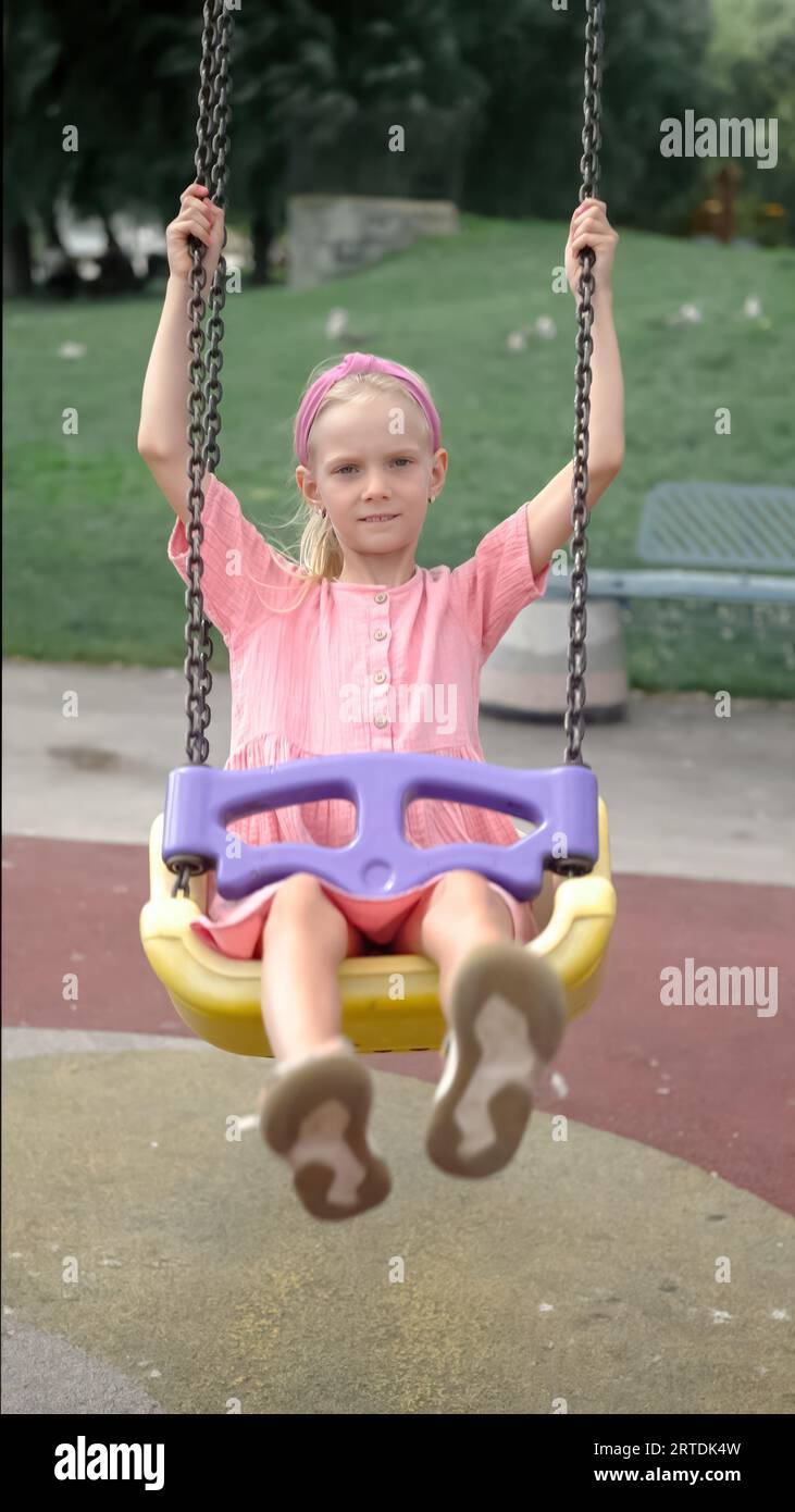 A joyful girl in a pink dress swings with delight in an urban park's ...