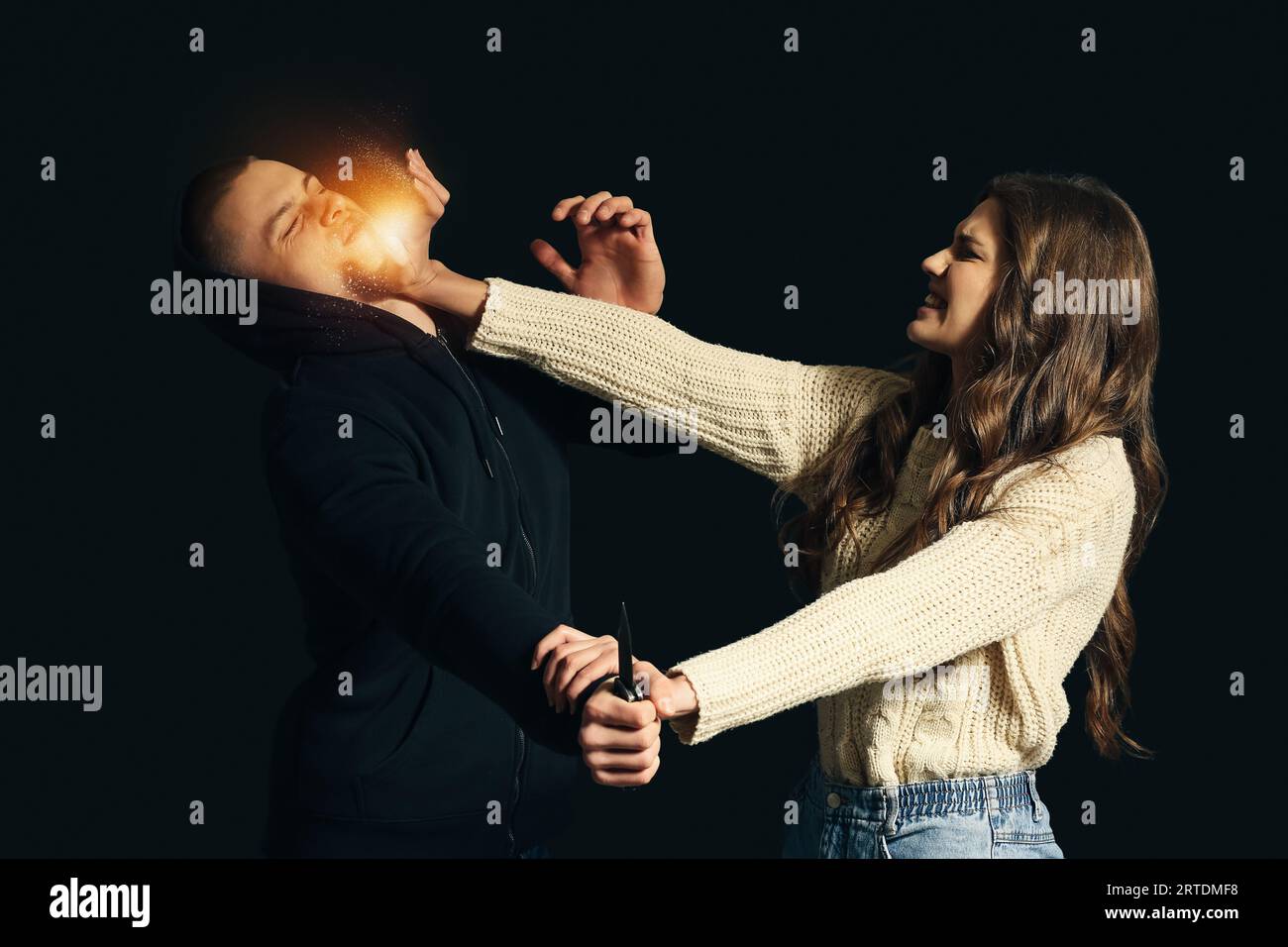 Young woman defending herself from attack by villain on dark background ...