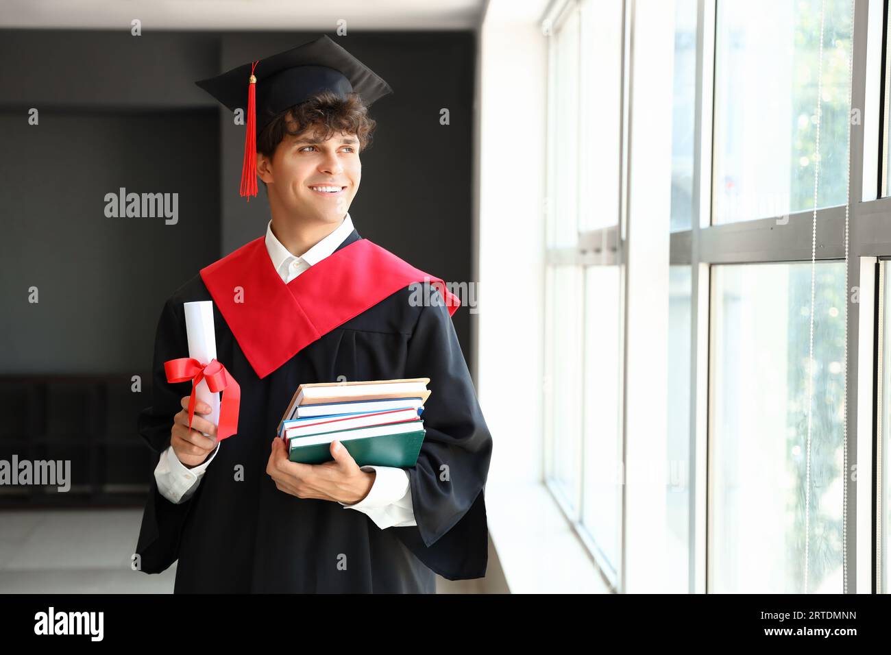 Male graduate student with diploma and books near window in room Stock ...