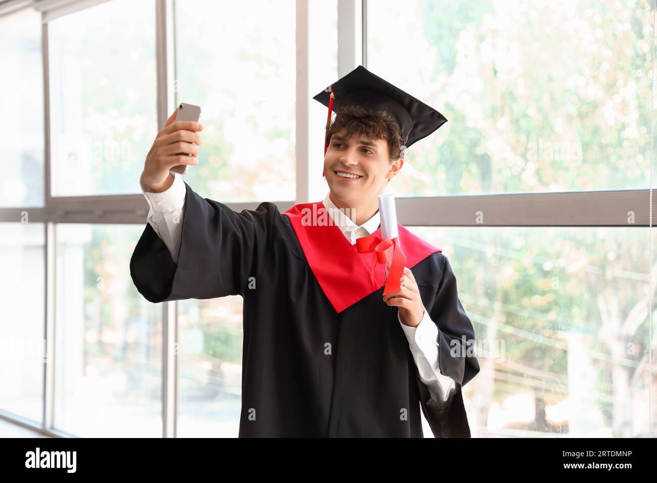 Male graduate student with diploma taking selfie near window in room ...