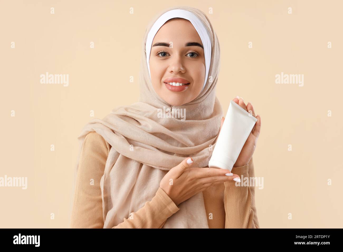 Young Muslim woman with tube of natural cosmetics on light background ...