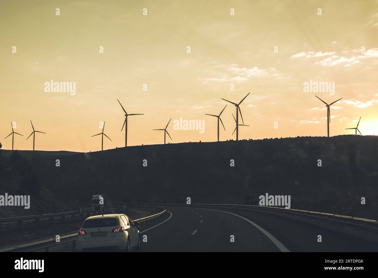 Wind turbines along a road, yellow sunset sky A road trip. Wind energy ...