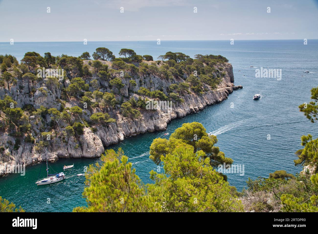 A boat in a calanque, green cliffs and red contrast. Blue water and sky ...