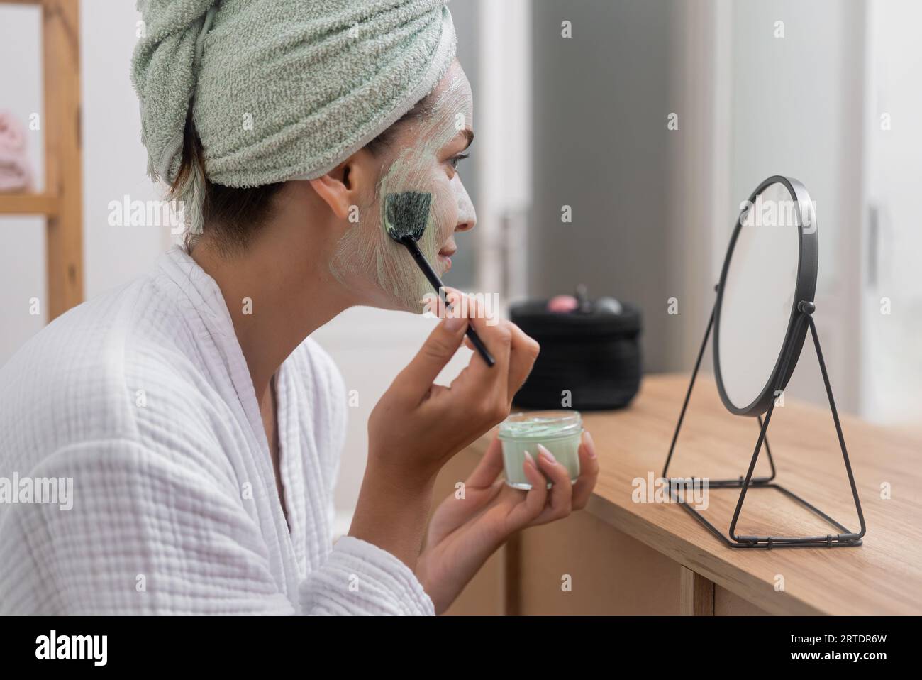 Wrapped in a towel, woman applies a facial mask to achieve anti-aging ...