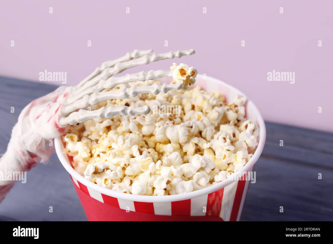 Popcorn bucket with Halloween skeleton hand on wooden table against ...