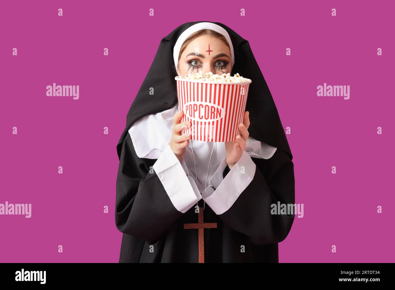 Young woman dressed for Halloween as nun with popcorn on color ...