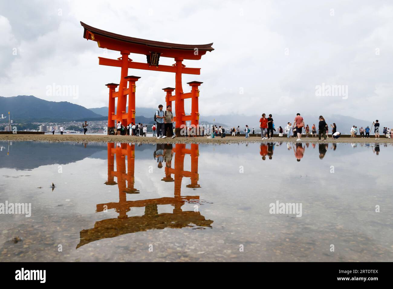 Tourists pose in front of a giant "torii" gateway at Itsukushima Shrine ...