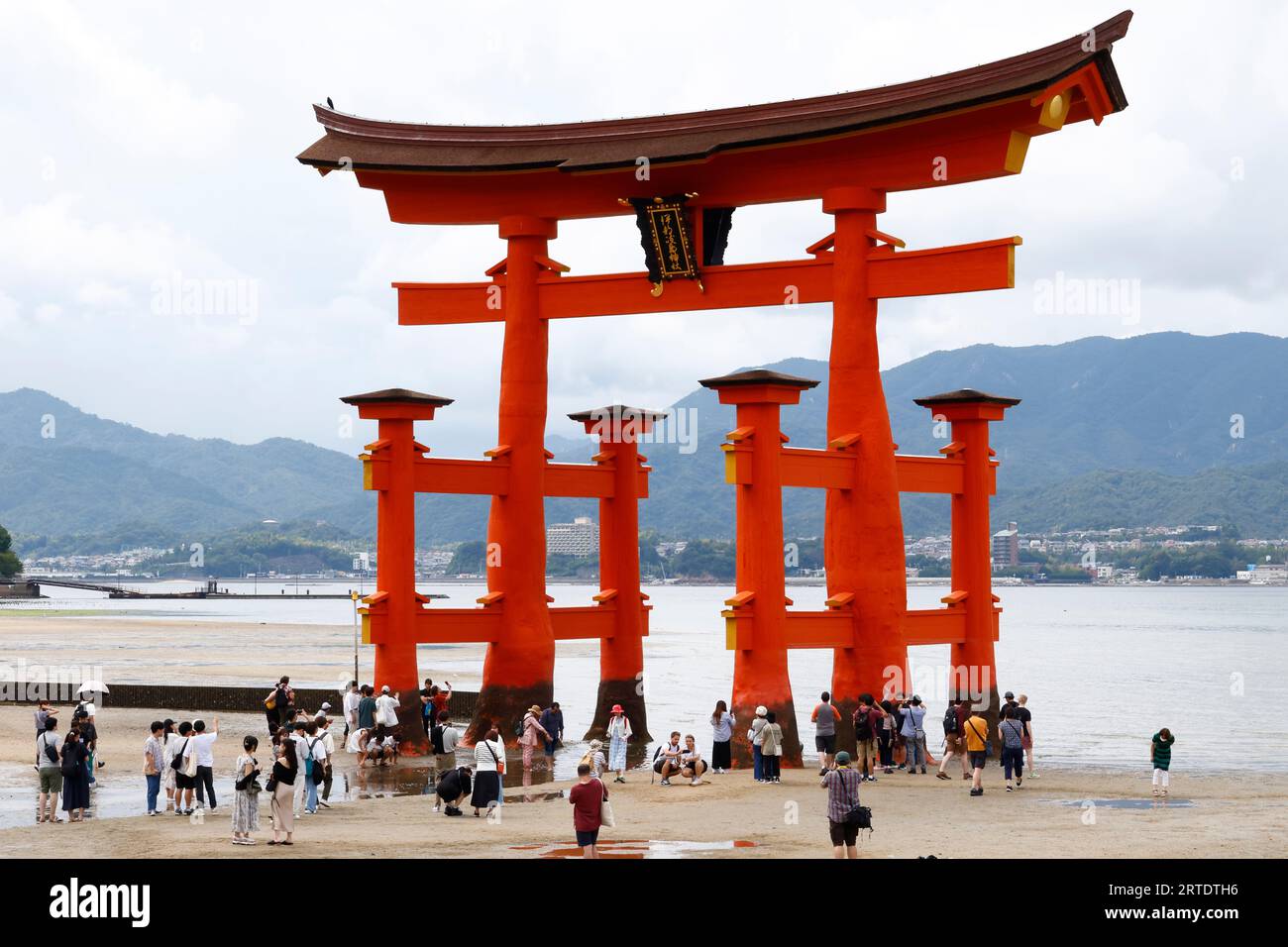 Tourists pose in front of a giant "torii" gateway at Itsukushima Shrine ...