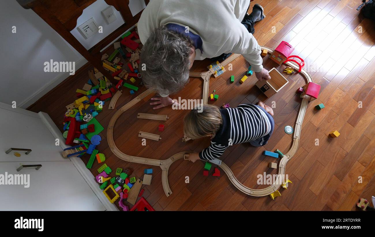 Little boy building train tracks with the help of his grandfather, seen ...